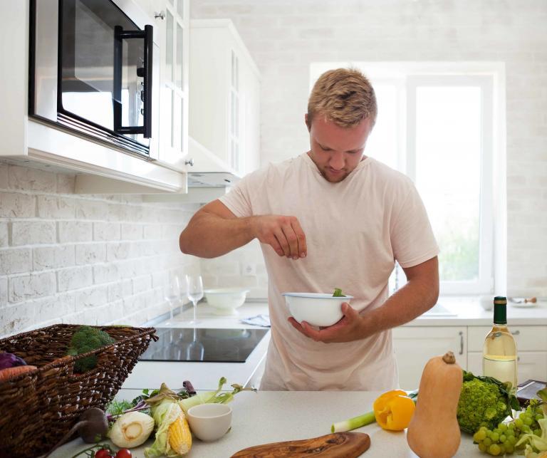 Handsome man cooking at home preparing salad in kitchen – Table at Home ...